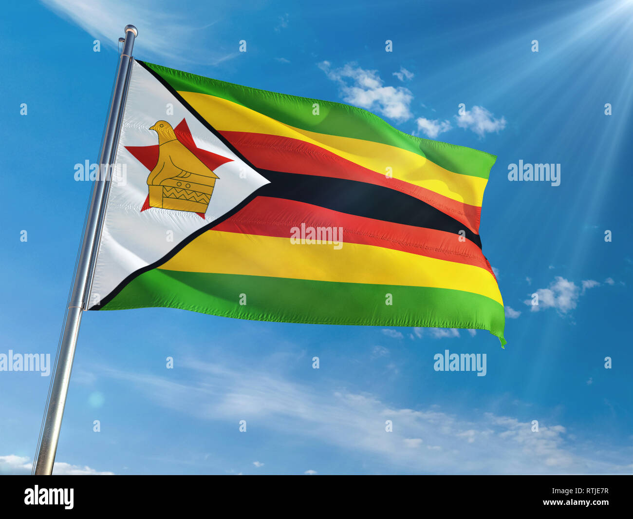 Zimbabwe National Flag Waving on pole against sunny blue sky background ...