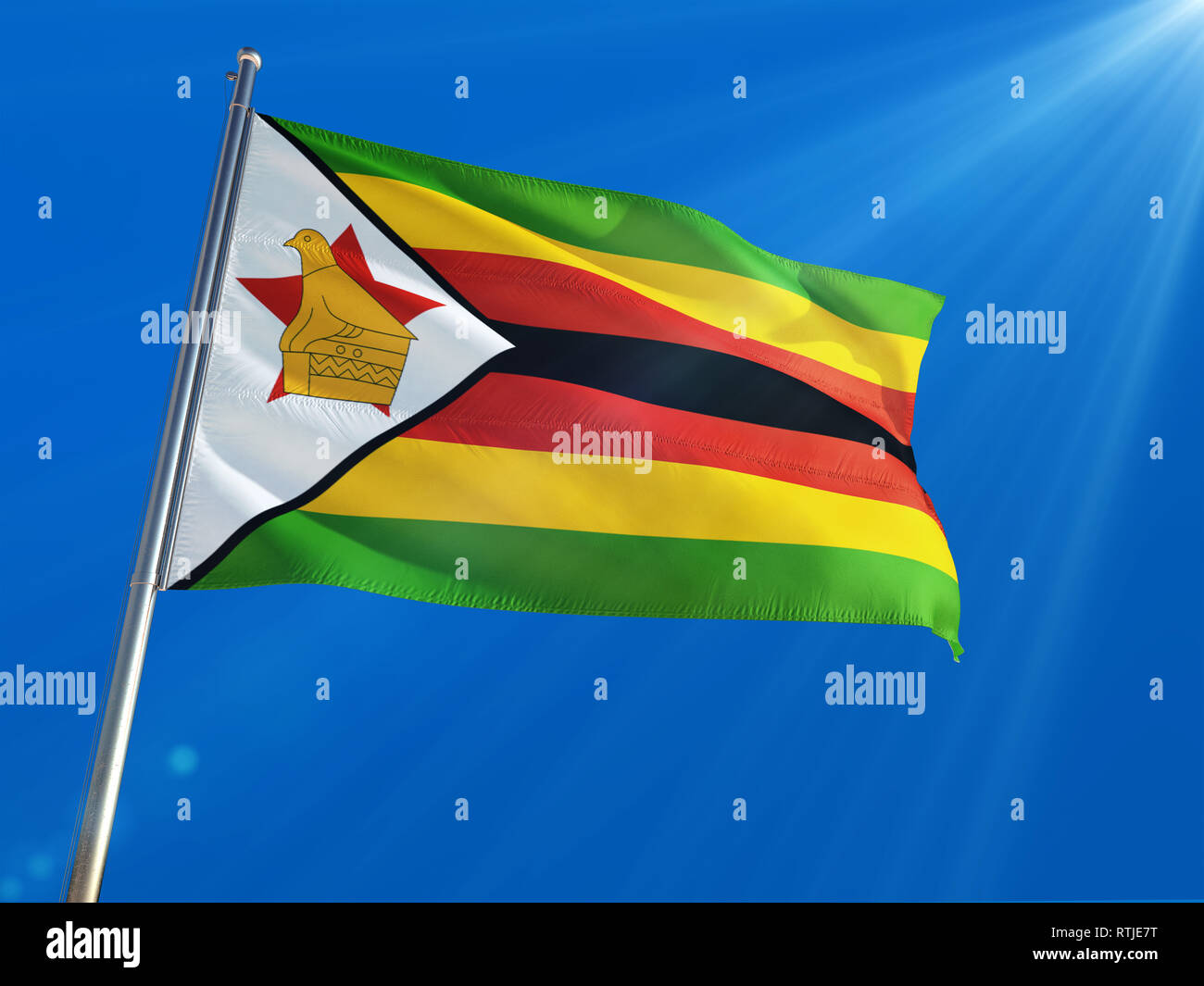 Zimbabwe National Flag Waving on pole against deep blue sky background ...