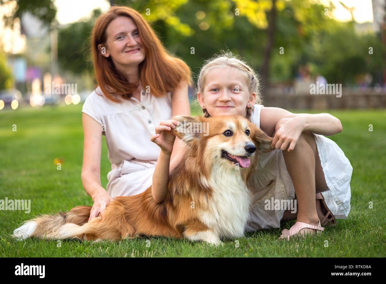 fun family - smiling mom and daughter and corgi fluffy sit on the lawn ...