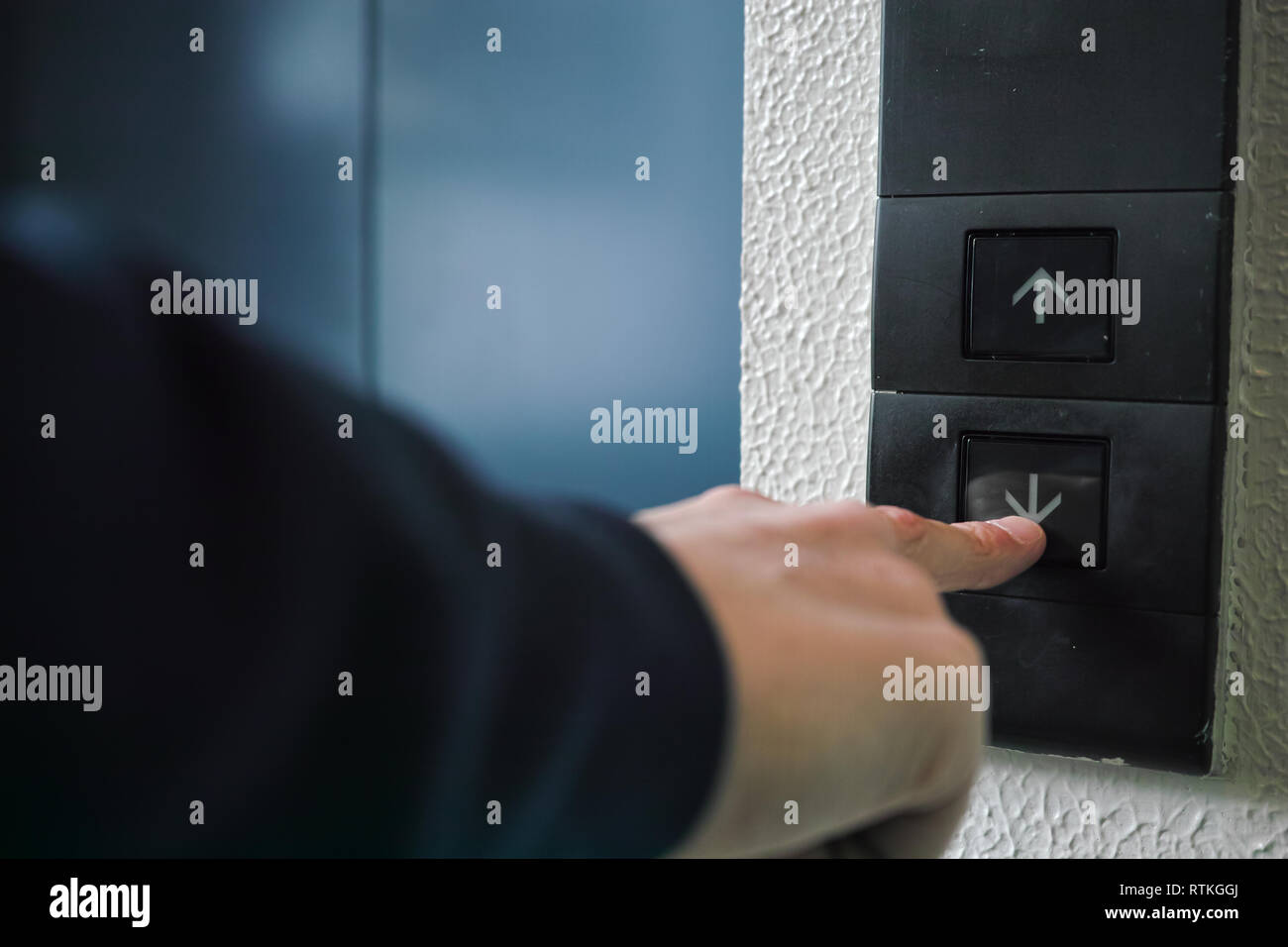 A rear view of a man pushing an elevator button with his index finger ...