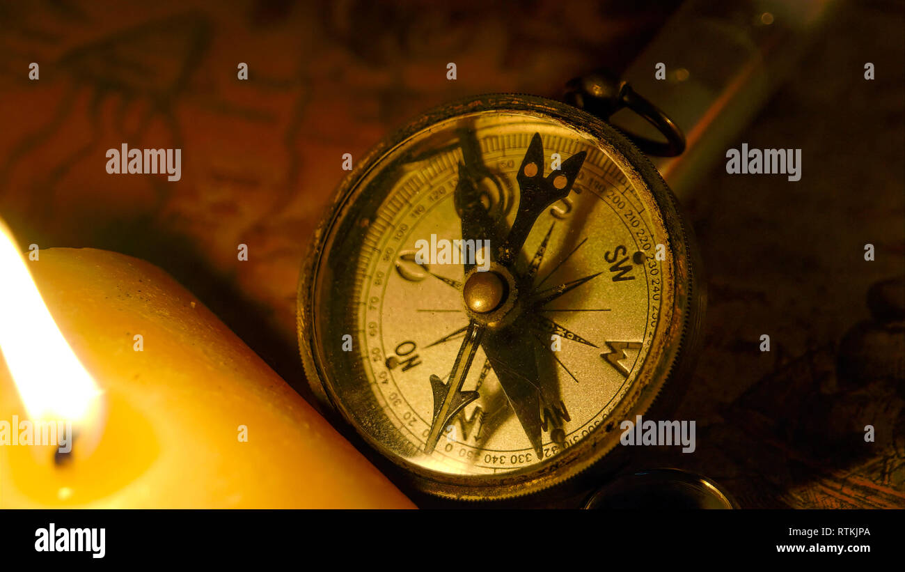 The compass beside the lighted candle on top of the navigational map ...