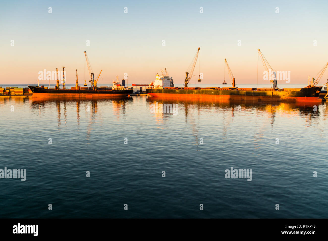 A cargo ship docks in the port, surrounded by an array of towering cranes and vividly colored ...