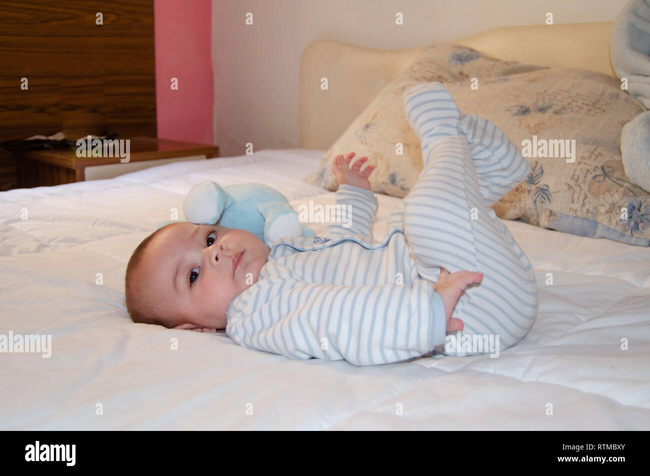 cute 4 months old baby boy lying on bed and playing with his legs ...
