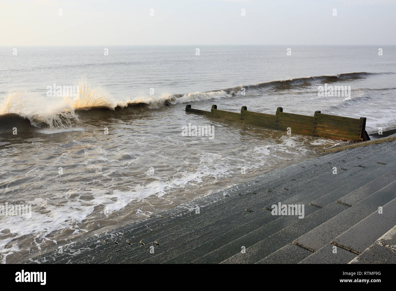Waves washing onto wooden groyne and concrete stepped revetment on ...