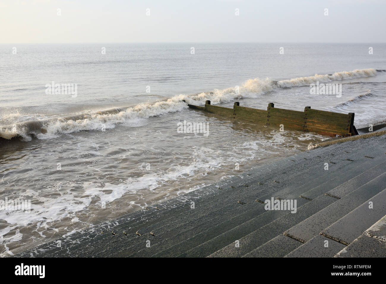 Waves washing onto wooden groyne and concrete stepped revetment on ...