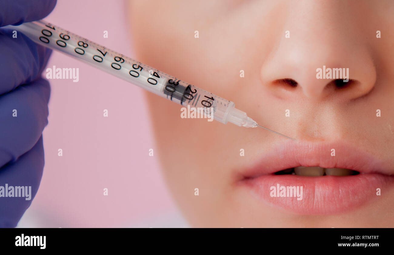 Doctor in gloves giving woman botox injections in lips, on pink ...