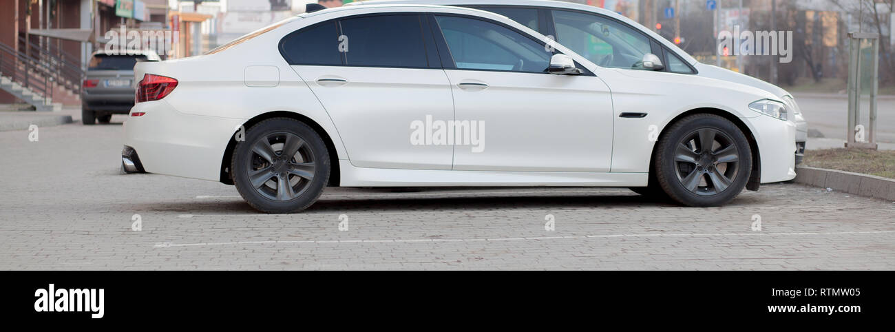 Side view of white car parked in paved parking lot area on blurred ...
