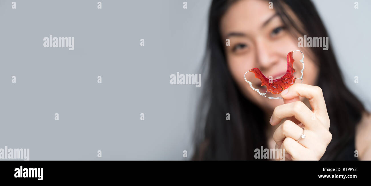 Portrait of beautiful Asian patient woman holding orthodontic retainers ...