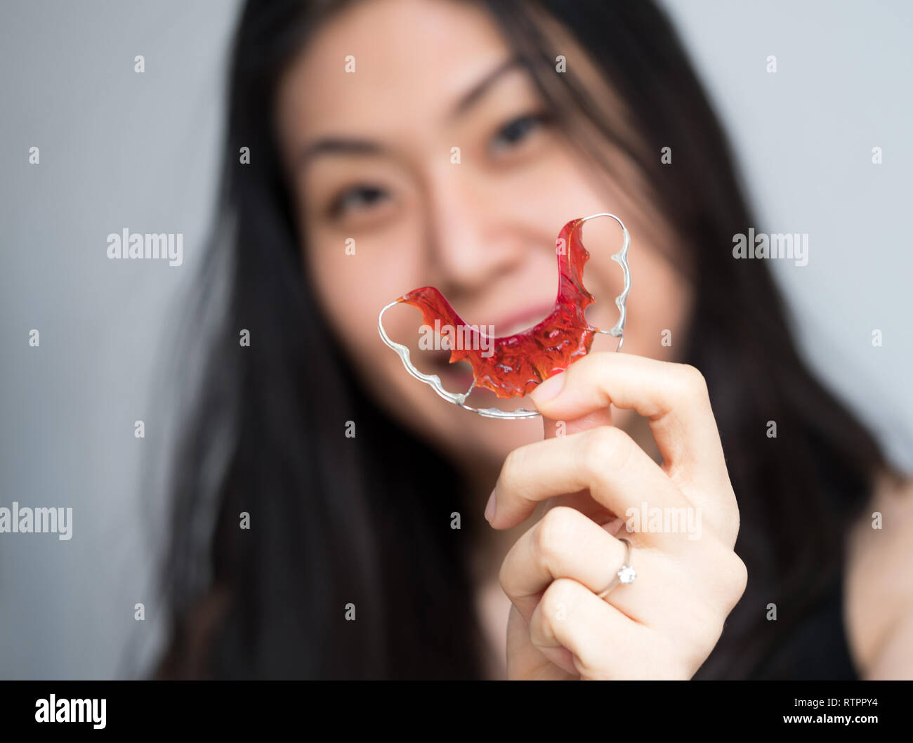 Portrait of beautiful Asian patient woman holding orthodontic retainers ...