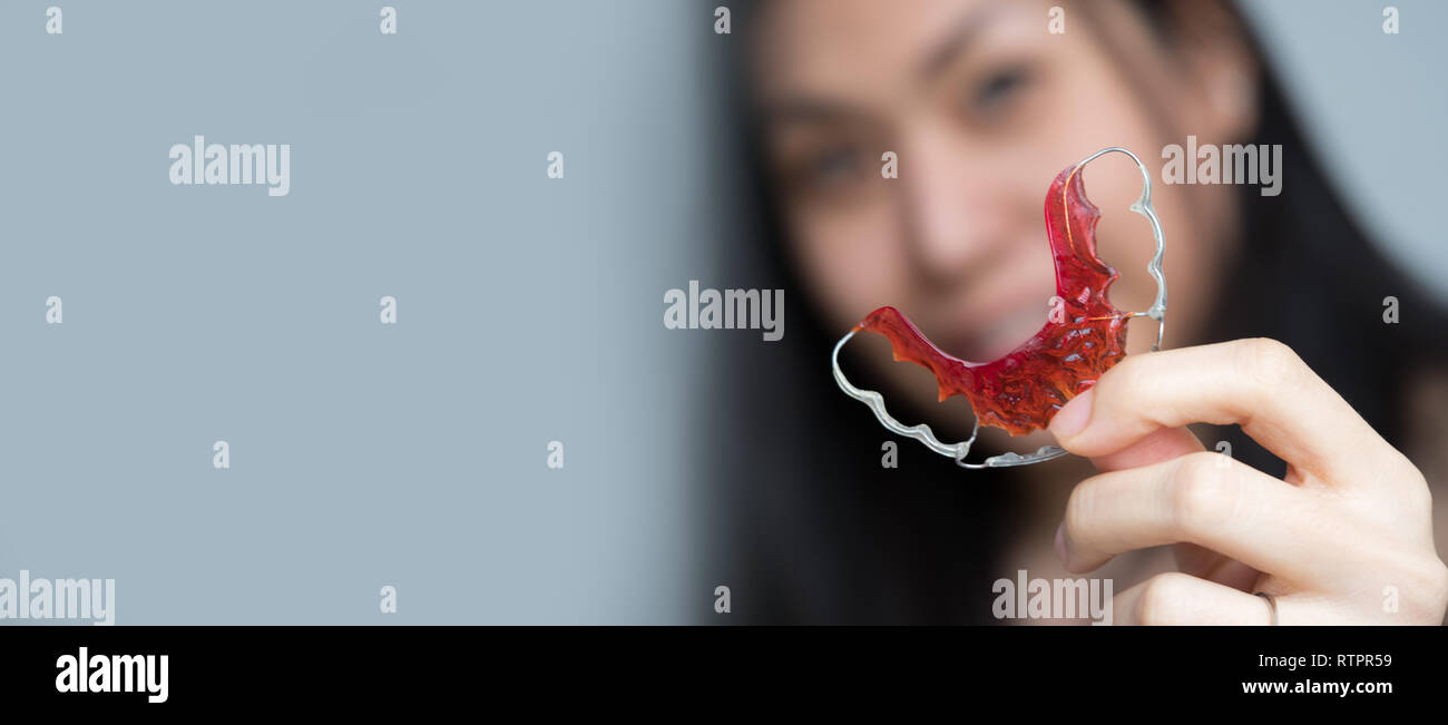 Portrait of beautiful Asian patient woman holding orthodontic retainers ...