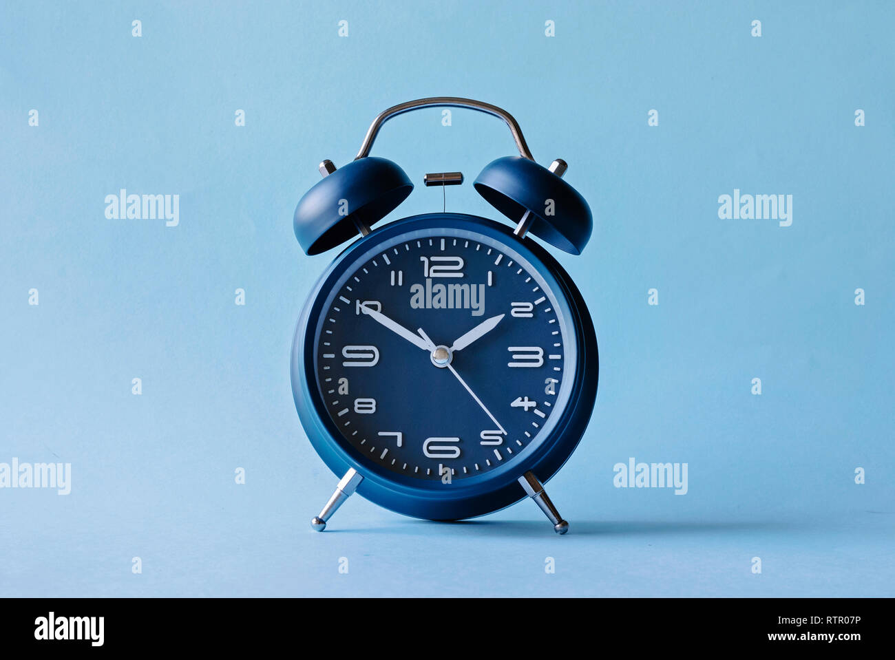 Retro style blue alarm clock with bells standing to the side over a ...