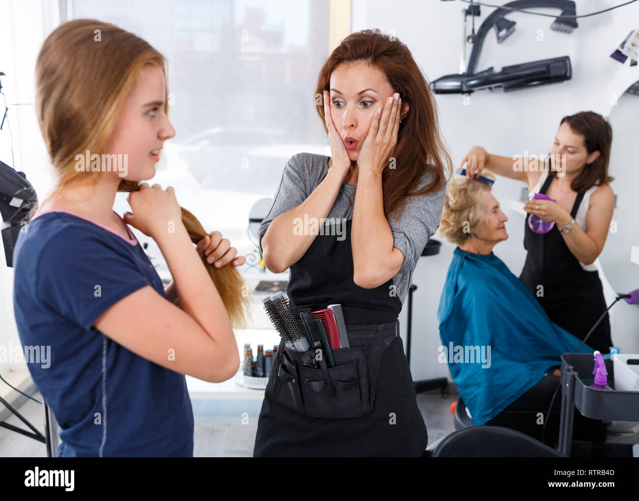 Shocked woman hairdresser looking at hair of young female client ...