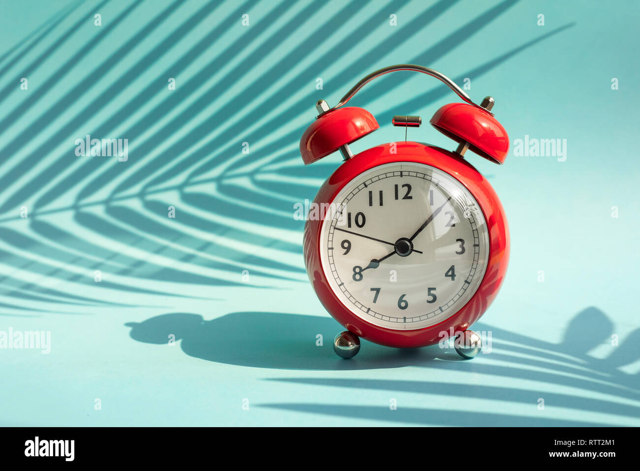 Summer time concepts idea with alarm clock and tropical leaf shadow on ...