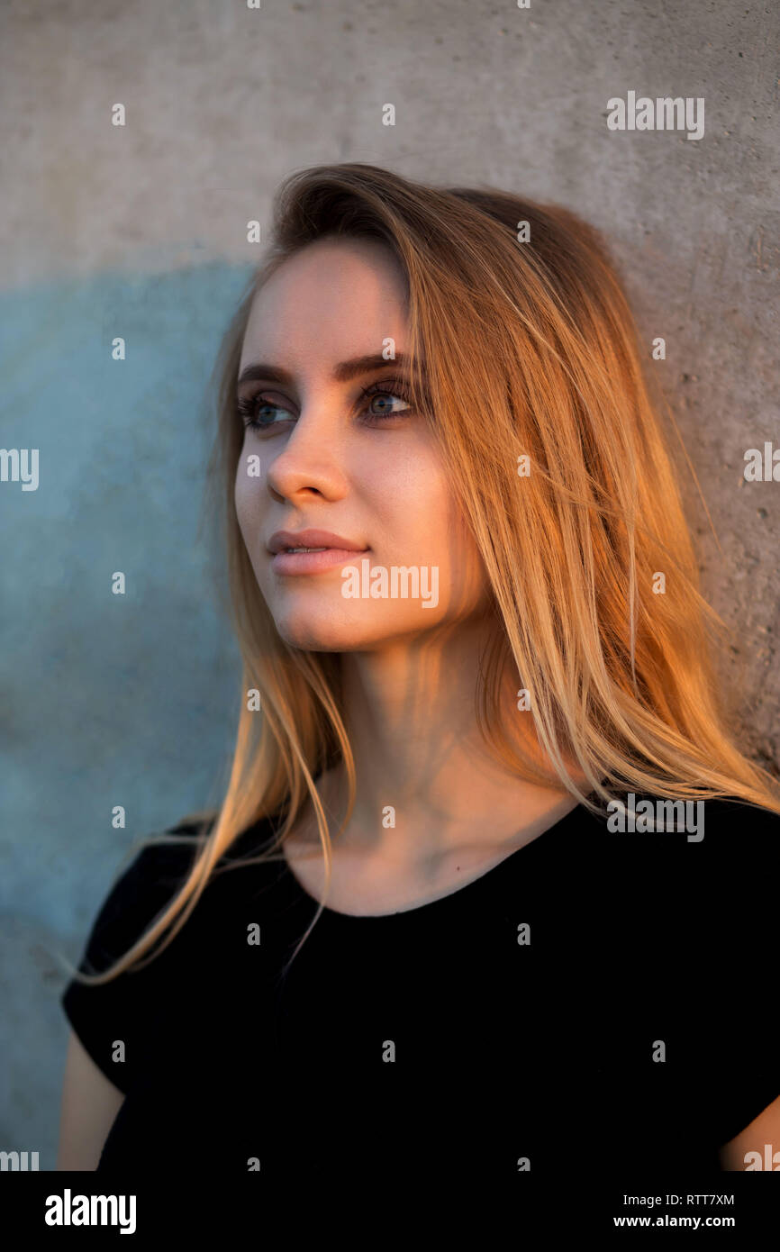 Sideways portrait of beautiful blonde woman in black top near wall of ...