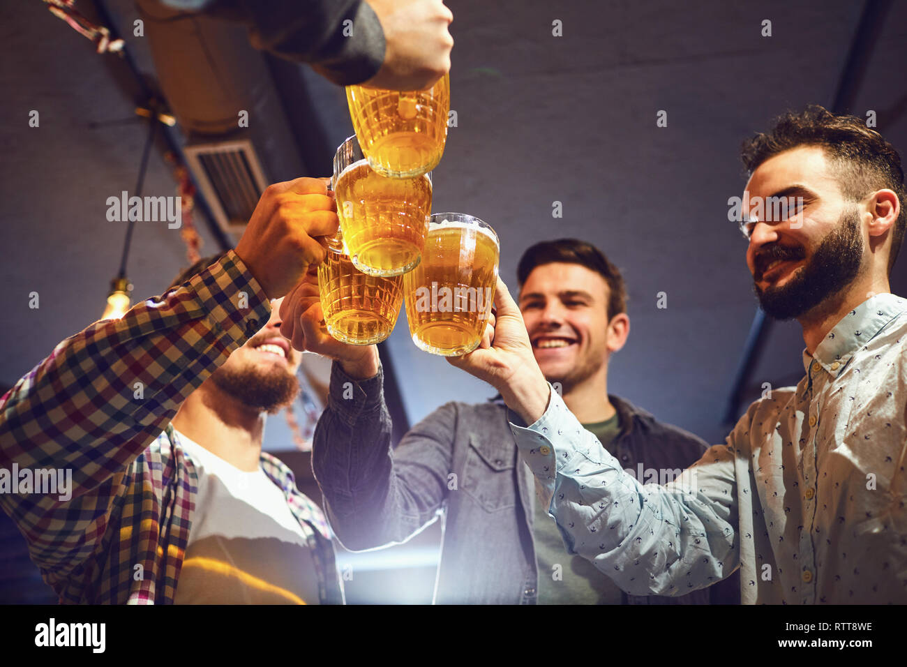 Young people clink glasses with beer in a bar Stock Photo - Alamy