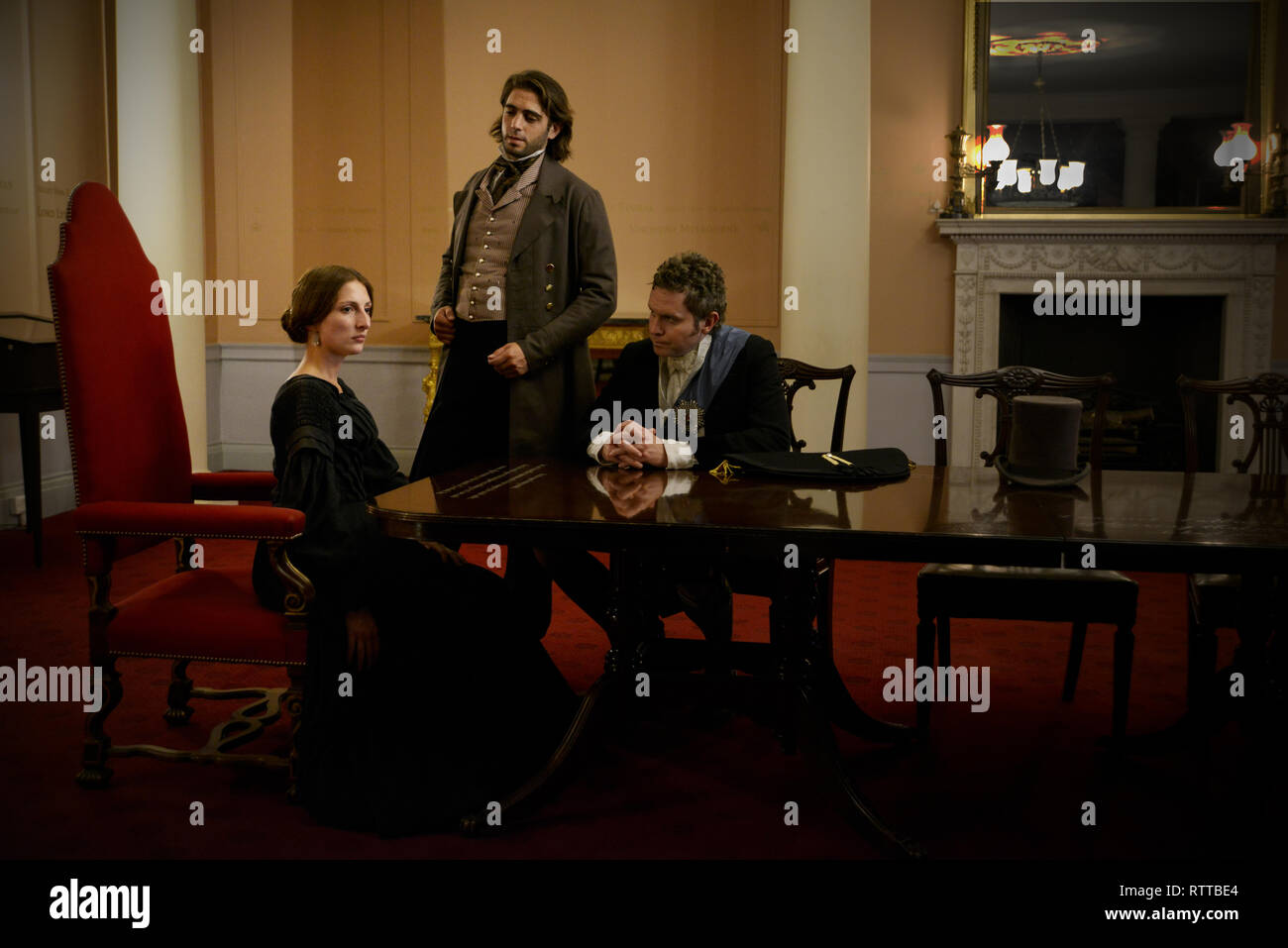 Queen Victoria and two gentlemen are deep in conversation in a dimly ...