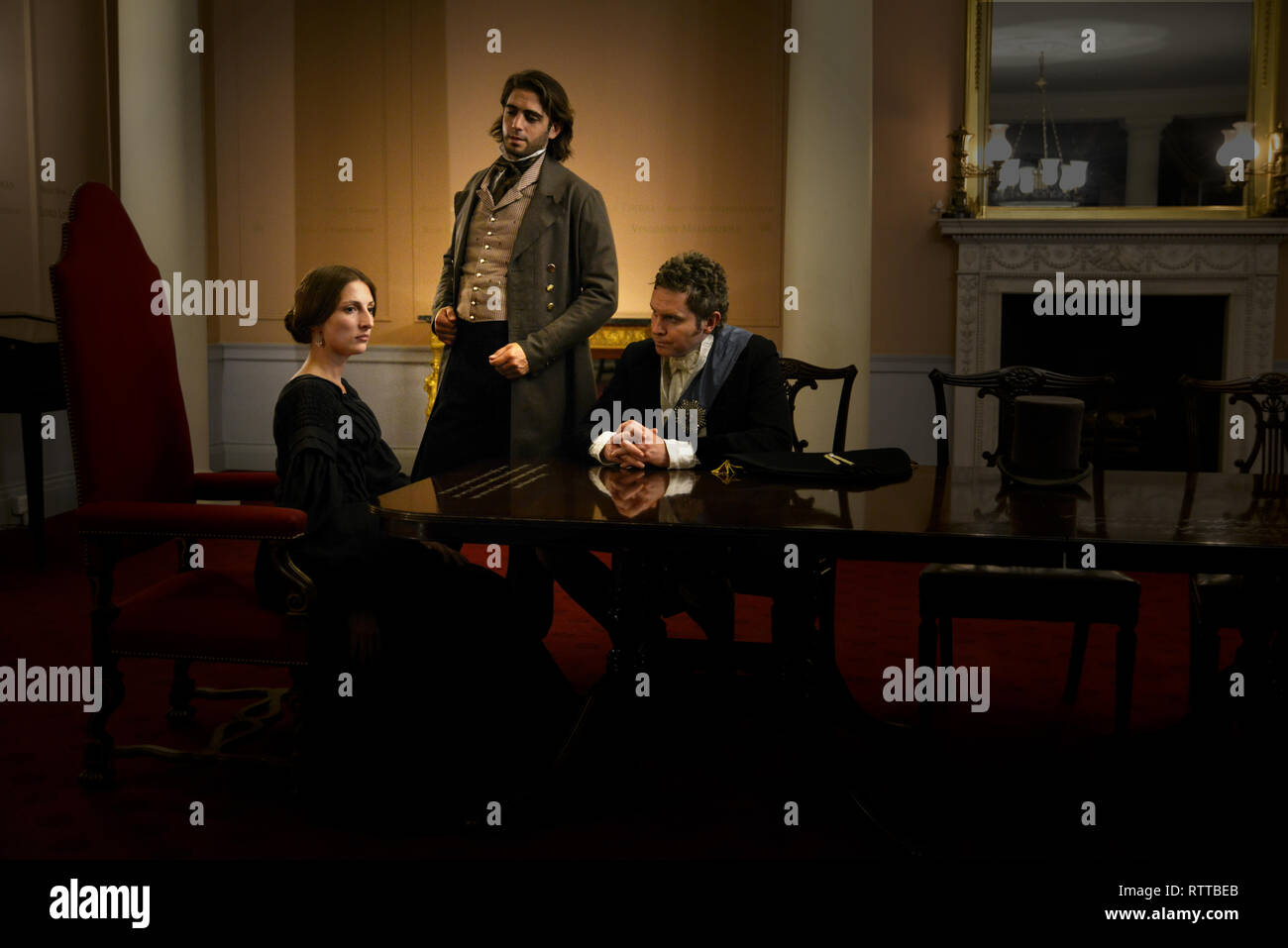 Queen Victoria and two gentlemen are deep in conversation in a dimly ...