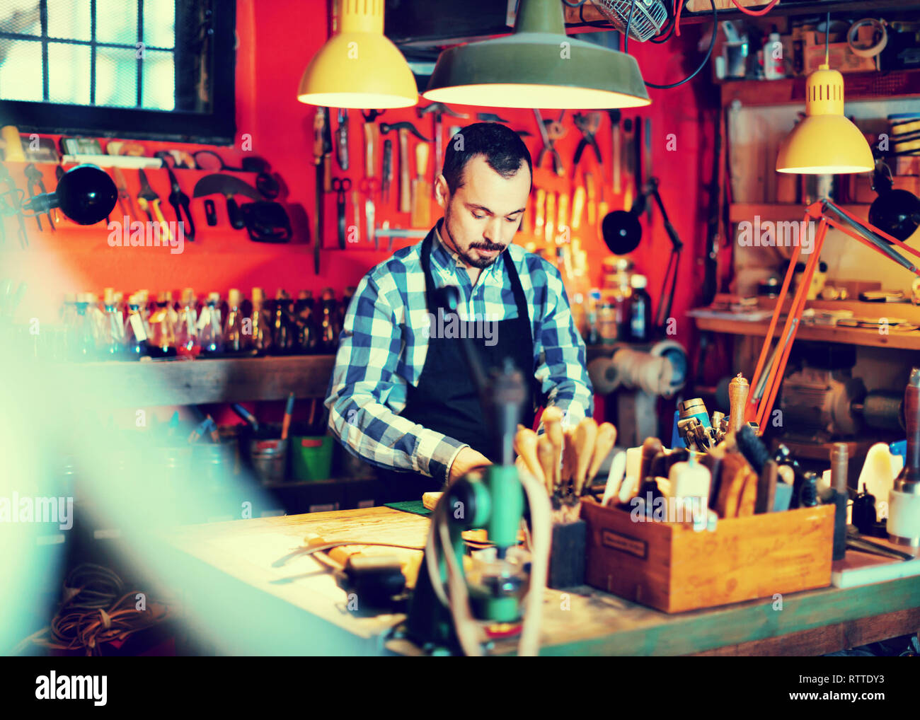 Diligent male worker working on leather for belt in leather workshop ...
