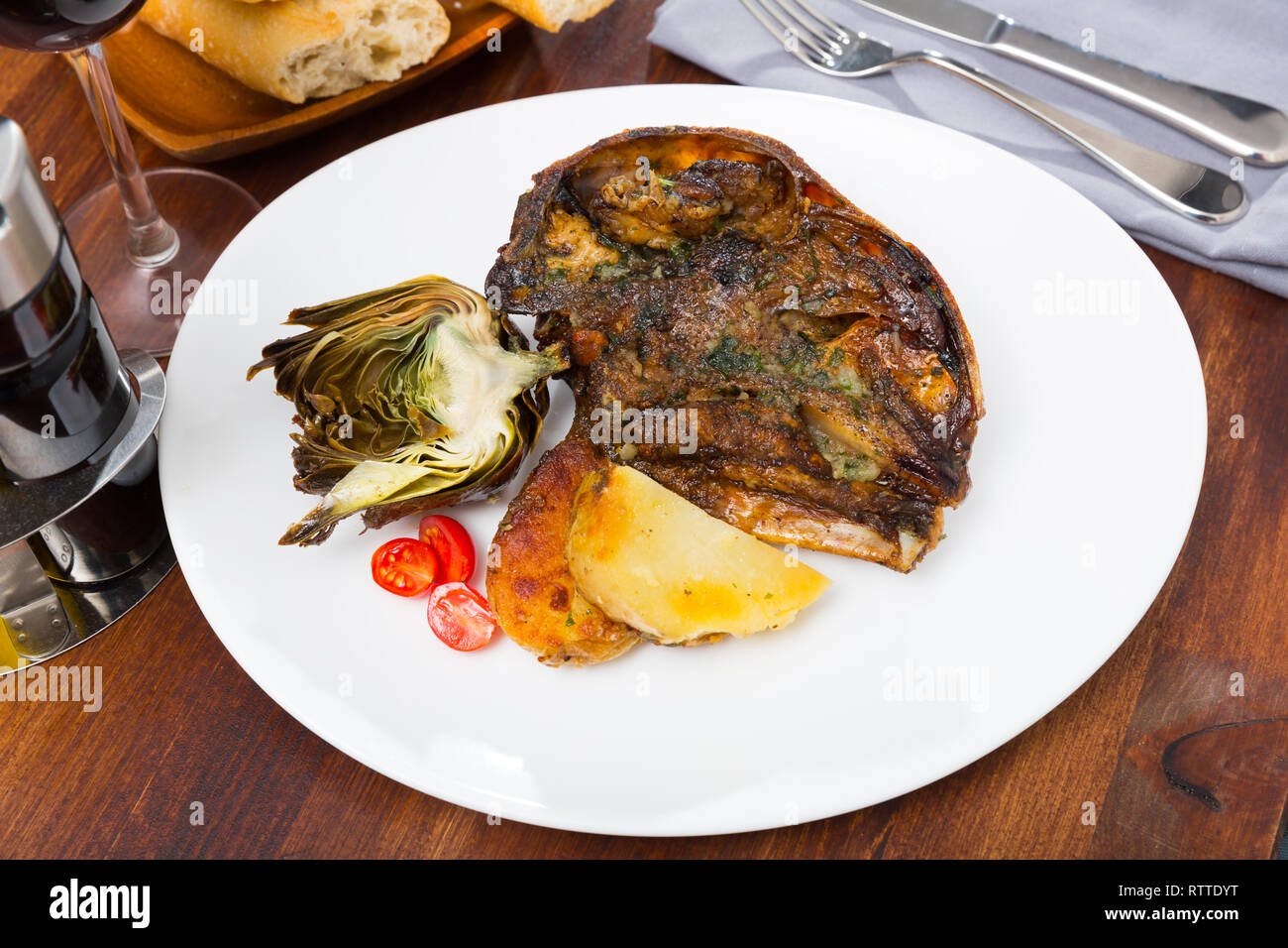 Roasted mutton head served with baked potatoes and halved artichoke and ...