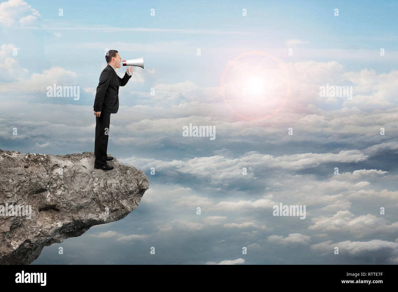 Businessman using megaphone yelling on cliff with sunlight cloudscape ...