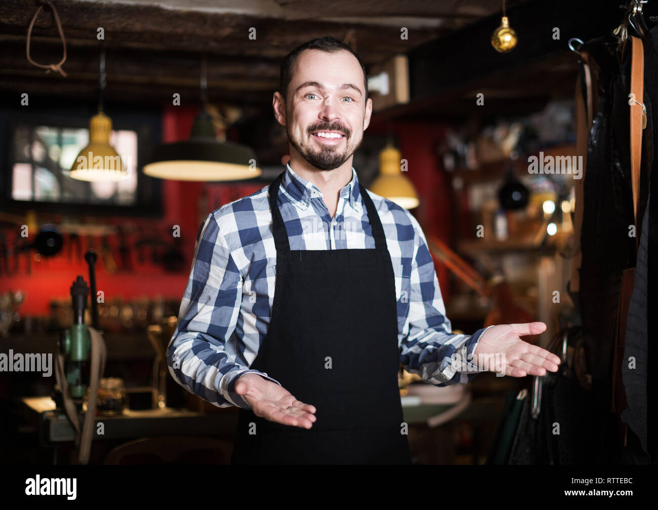 Smiling male worker demonstrating his workplace and tools in leather ...