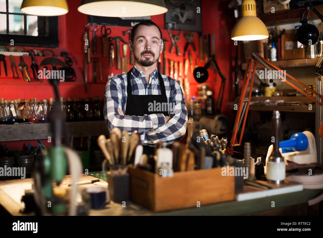 Attractive male worker demonstrating his workplace and tools in leather ...
