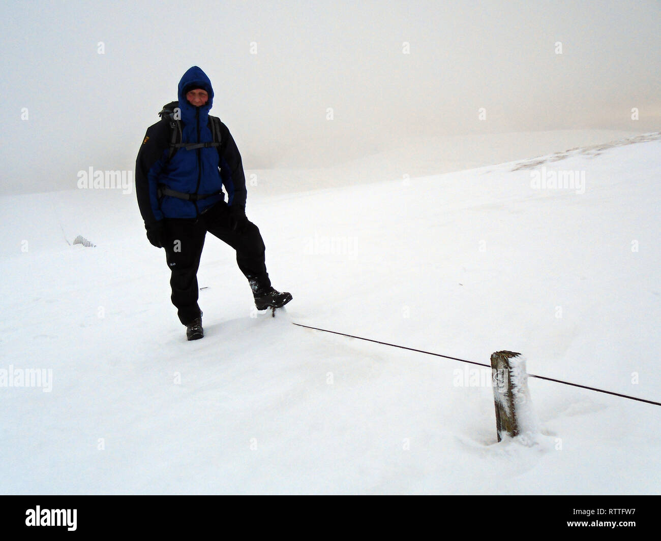 Lone Male Hiker Standing in Snow on Fence Post on Route to the Scottish ...