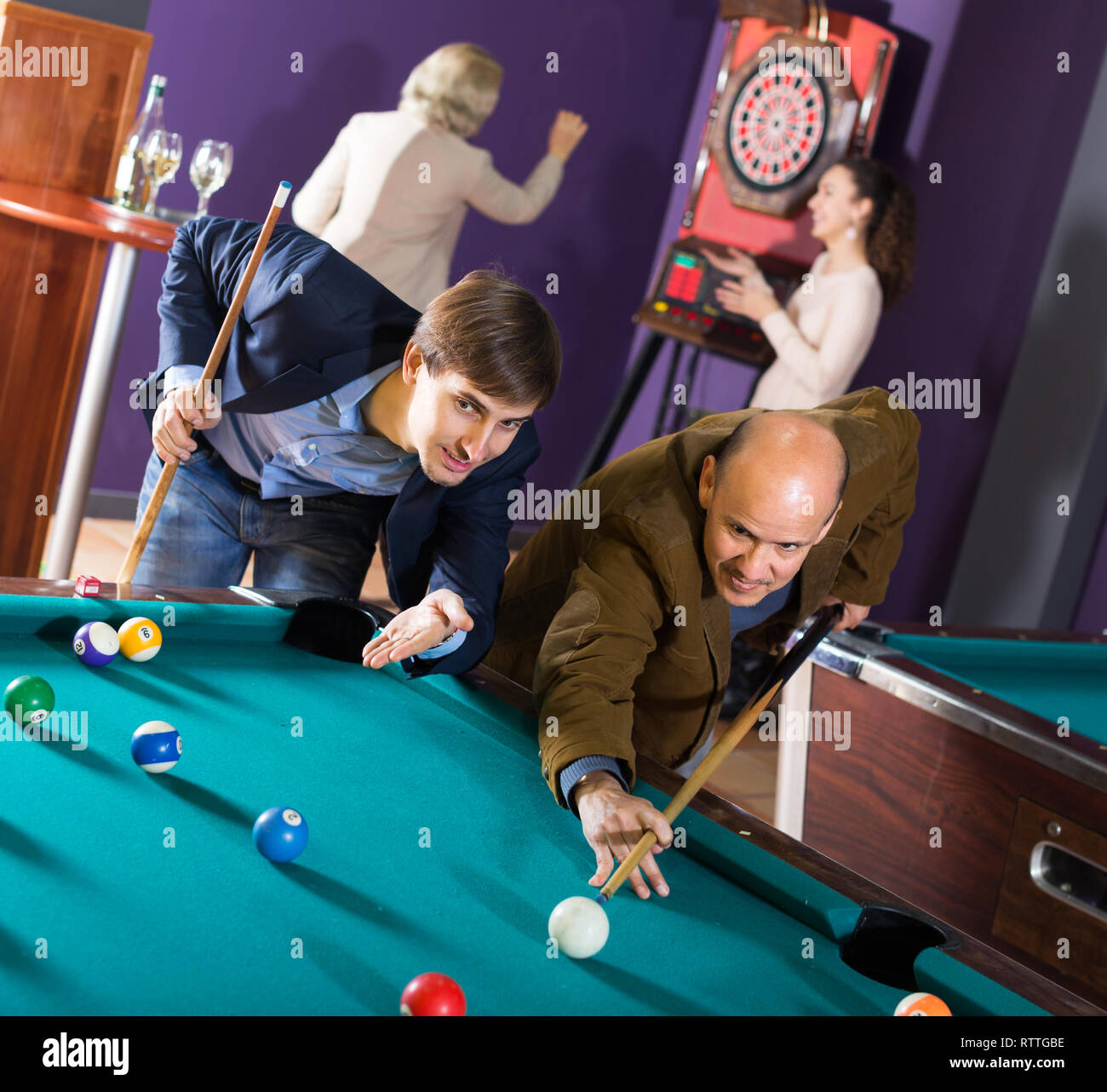 Relaxed smiling adult people playing billiard and darts as hanging out ...