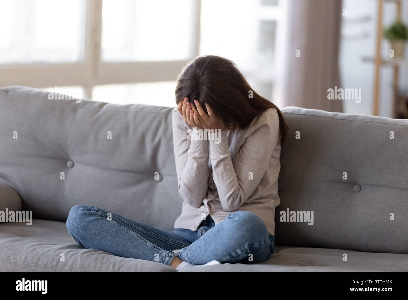 Depressed young woman covering face by hands, crying alone at home ...
