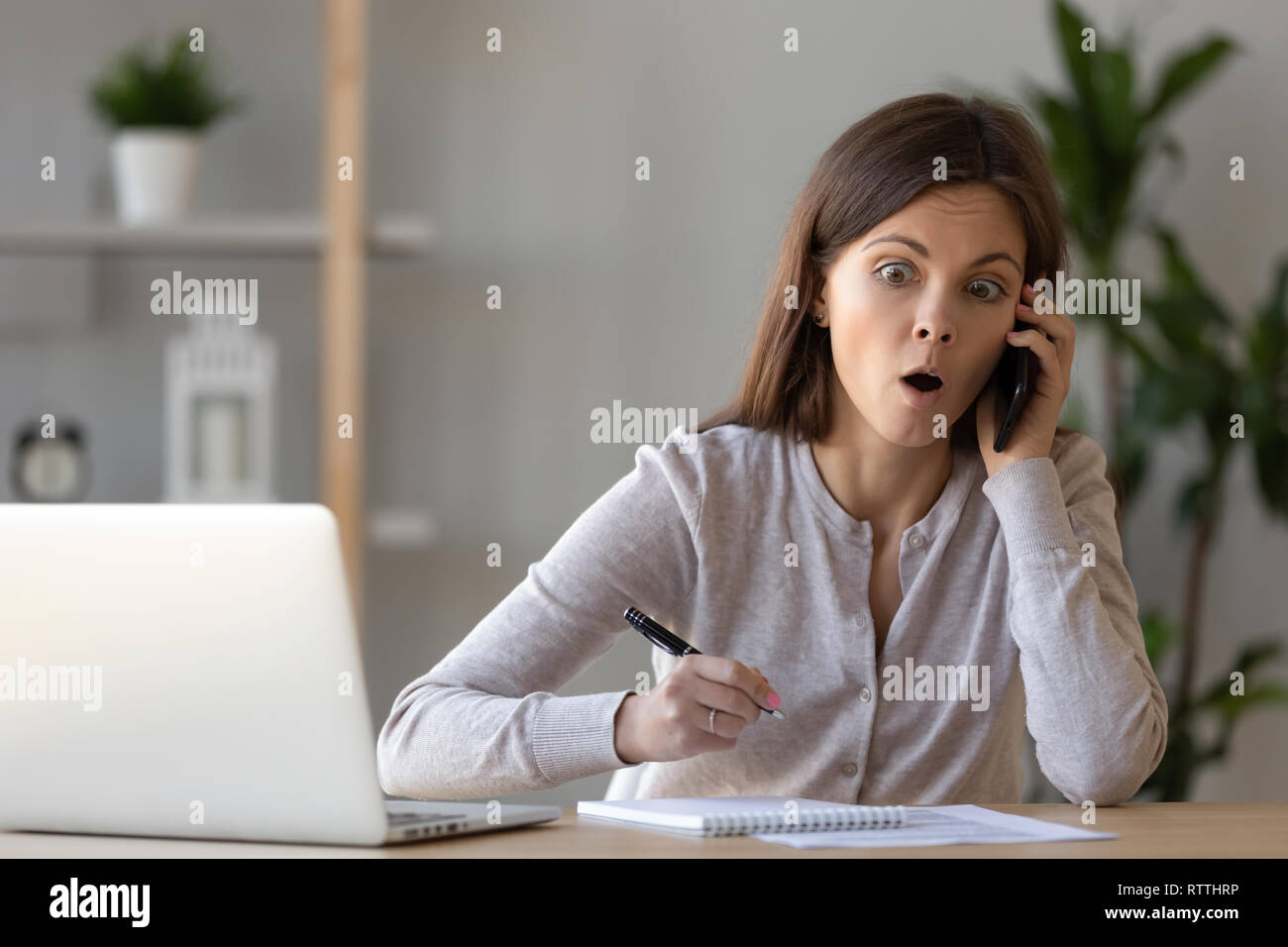 Shocked woman talking on phone, hearing amazing news, writing notes ...