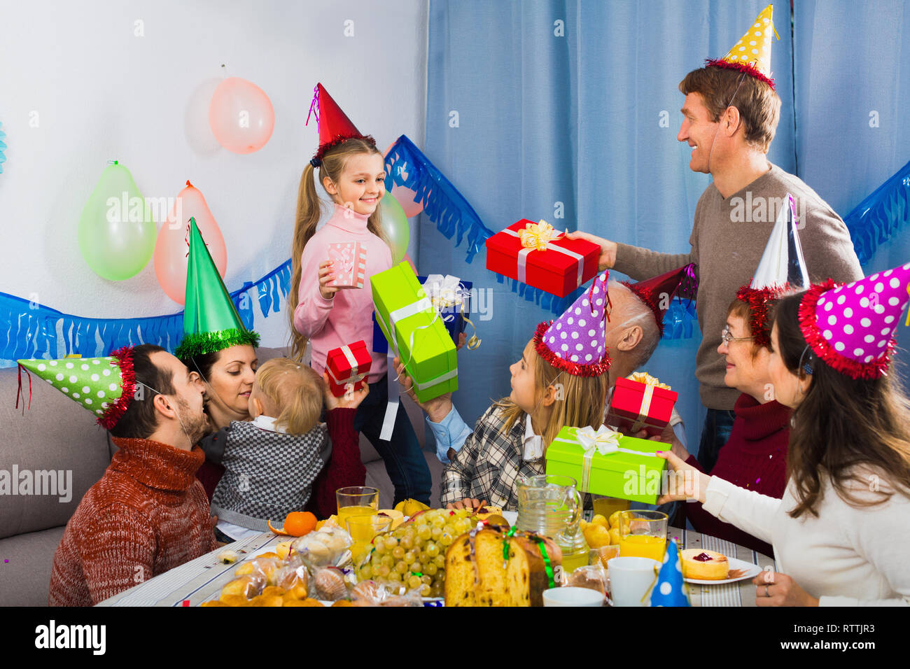 Large positive smiling family presenting gifts to girl during birthday ...