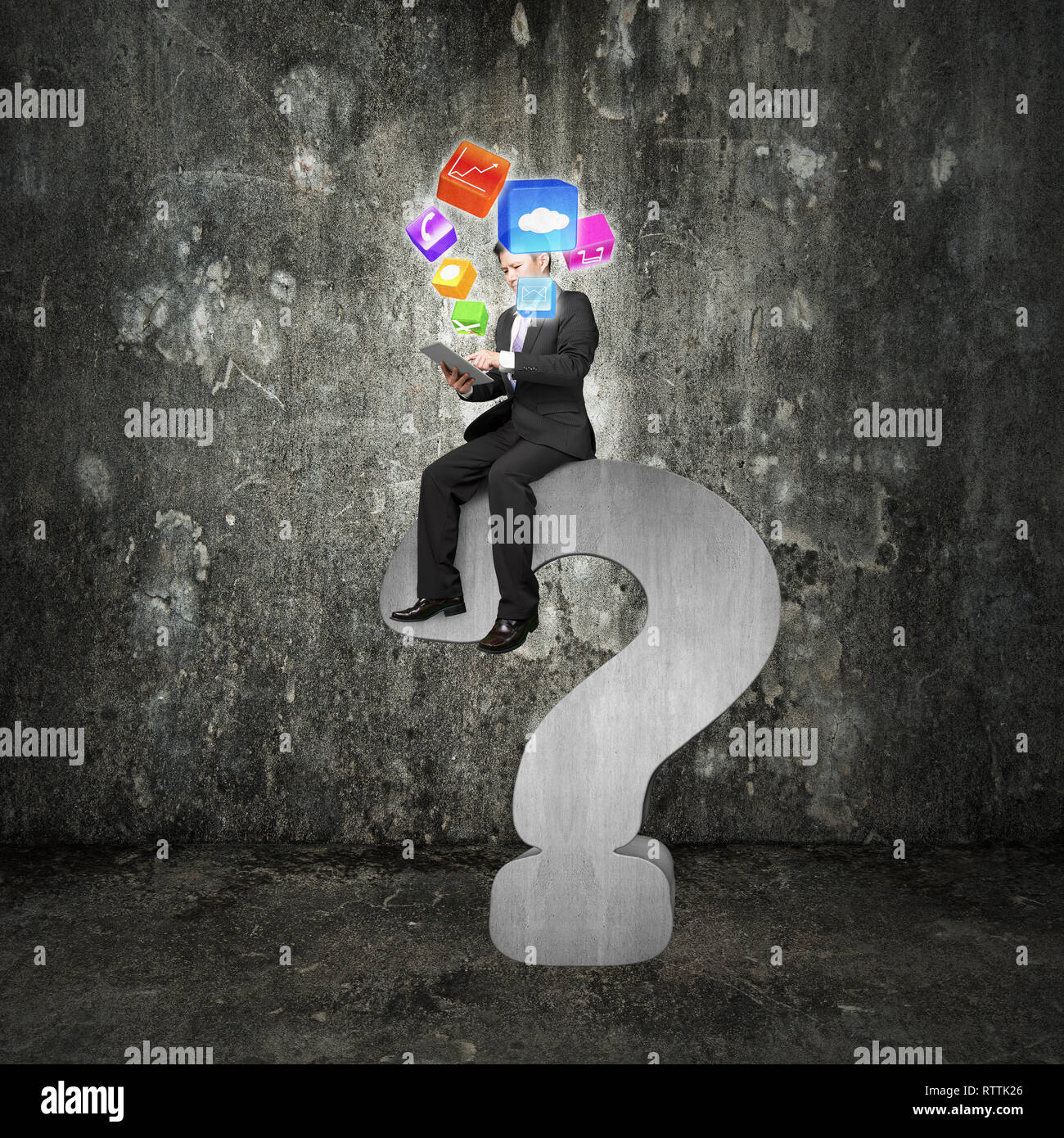 Businessman using tablet sitting on gray question mark with app icons and concrete room ...