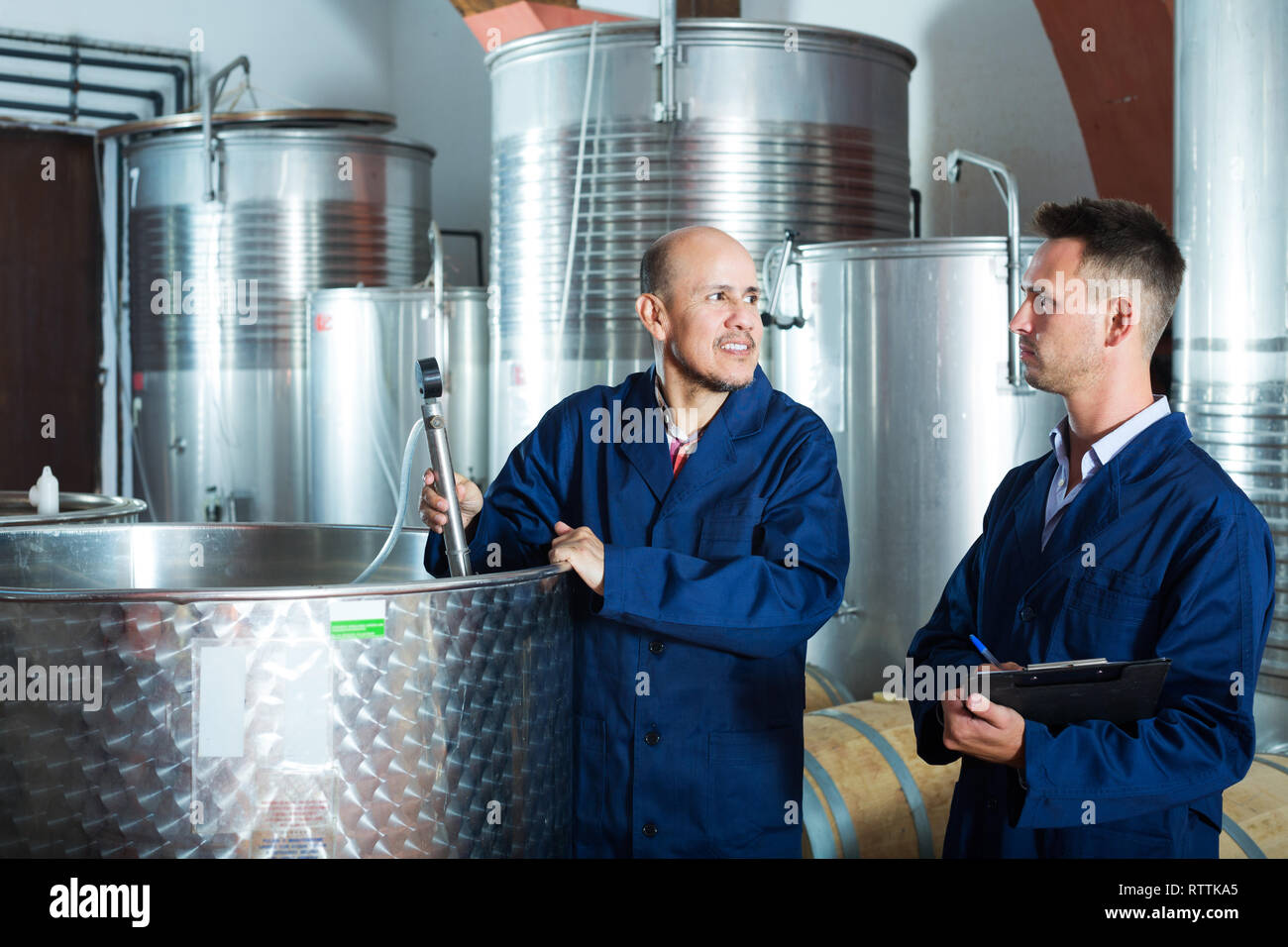 Young serious winery workers taking notes while checking equipment in ...