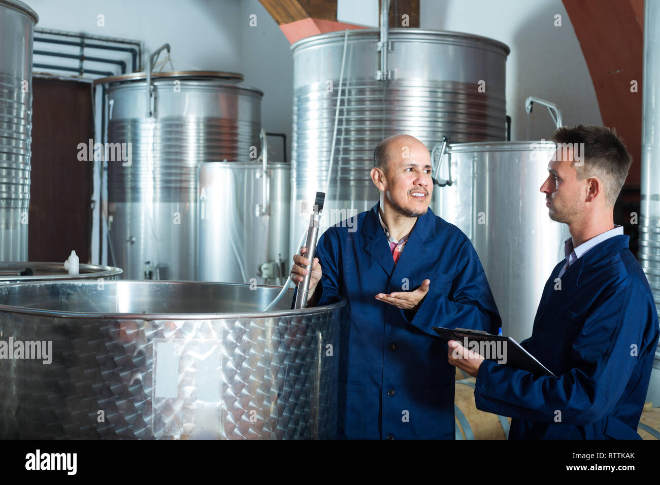 Two positive male winery workers in uniform working and taking notes in ...
