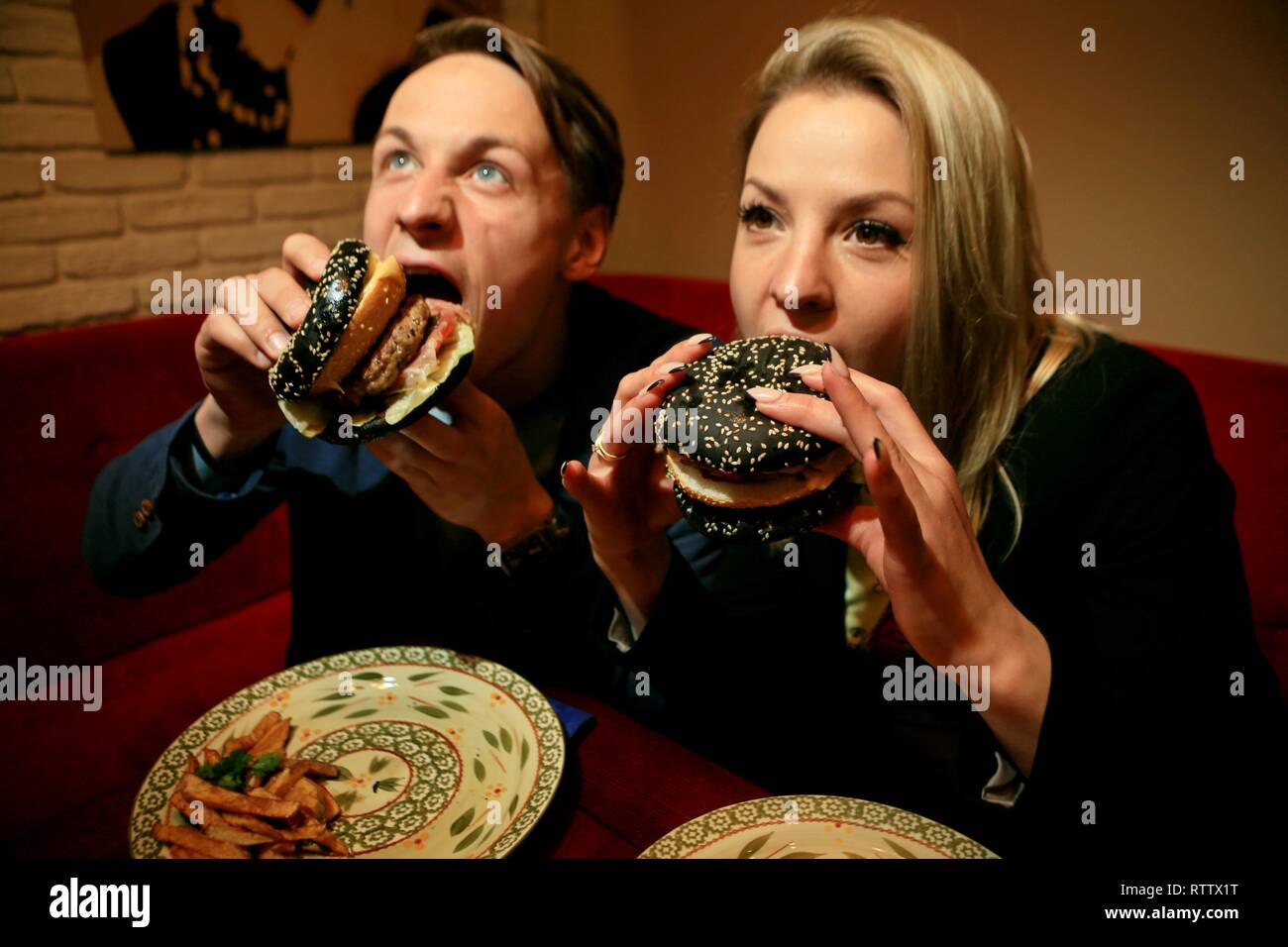 The guy and the girl eat cheeseburger with black bread, beef patty ...