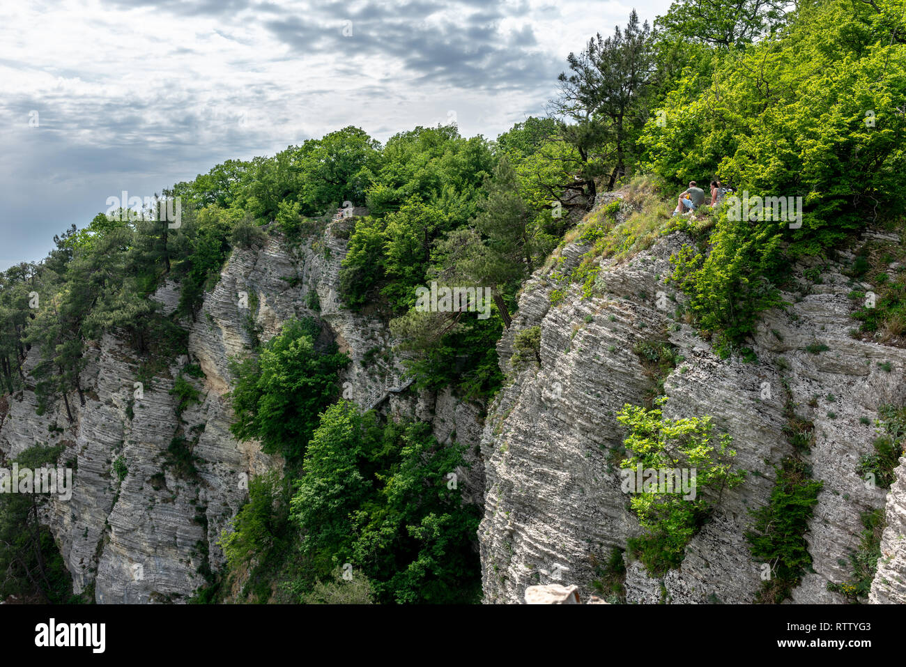 Mountain with a steep green rocky slope. Several people are extremely ...
