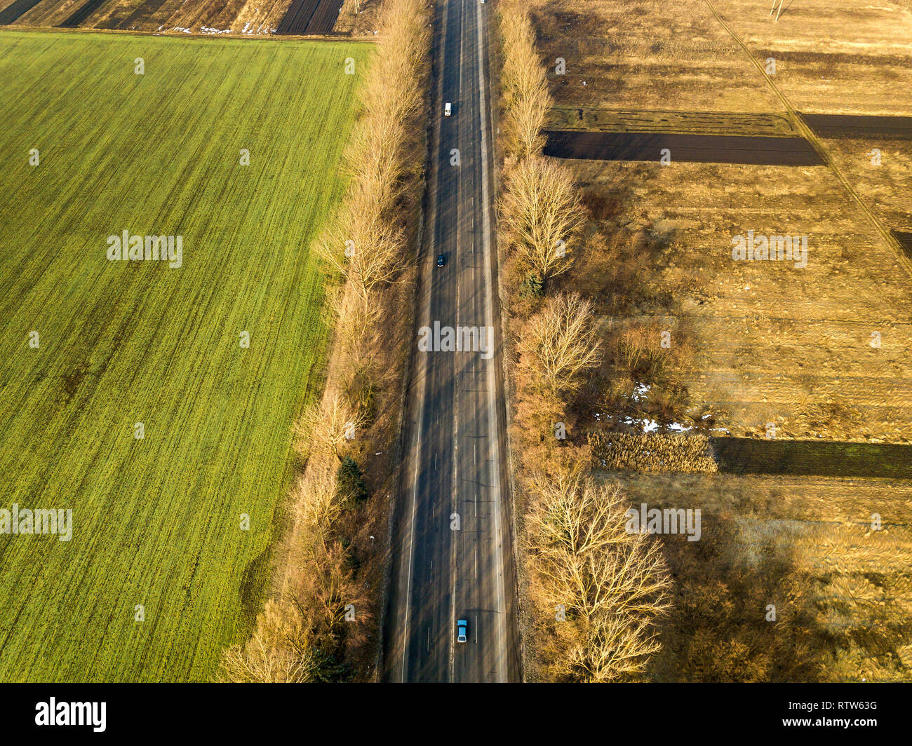 Aerial view of straight road with moving cars, trees and green fields ...