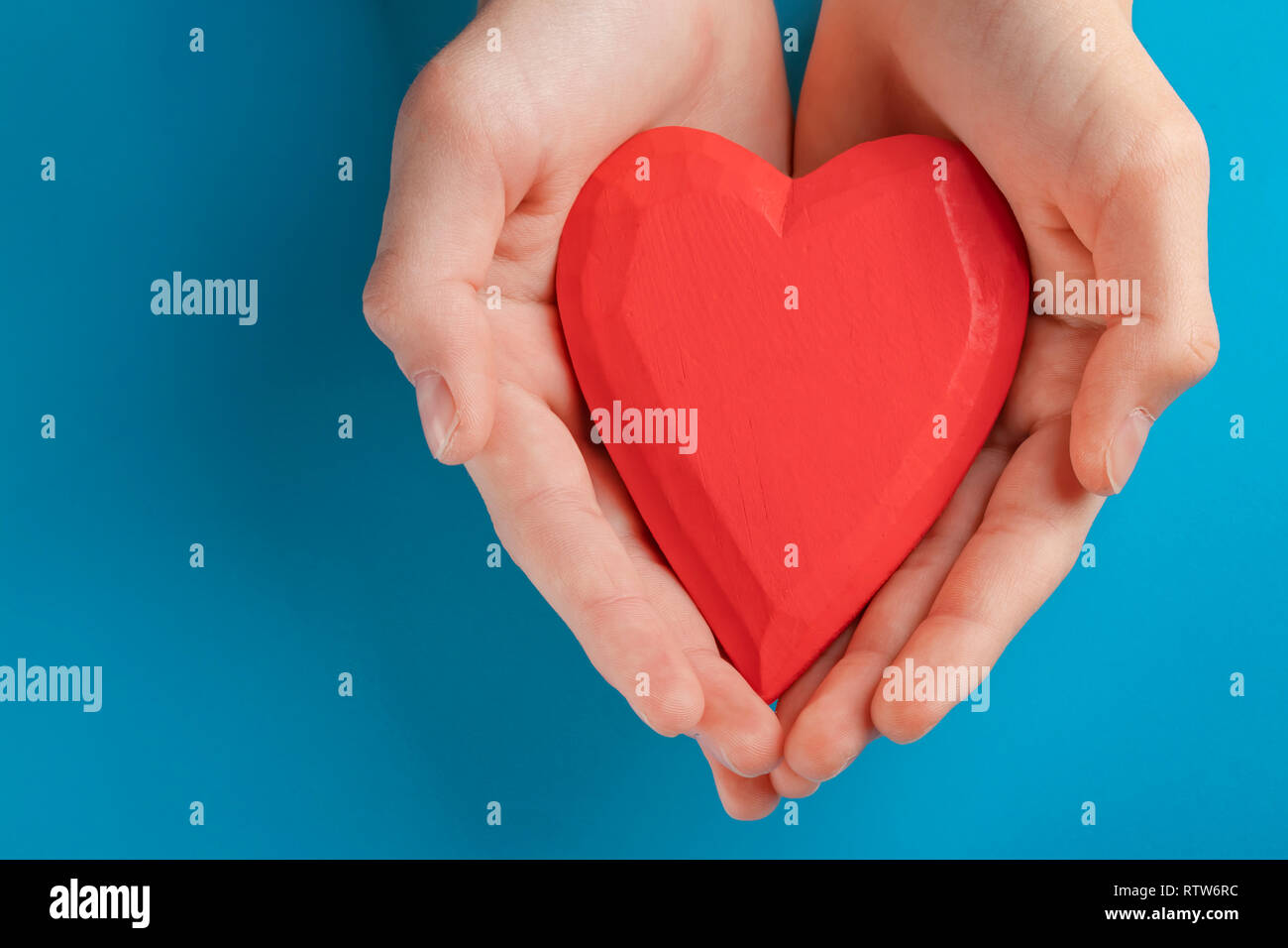 Hands of a teenager child holding a red wooden heart in their hands ...