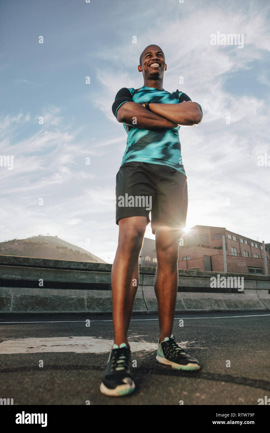 Smiling male runner standing on the street in morning with his arms ...