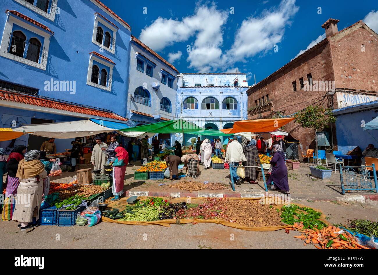 Locals shopping for vegetables and fruit, market in front of blue ...