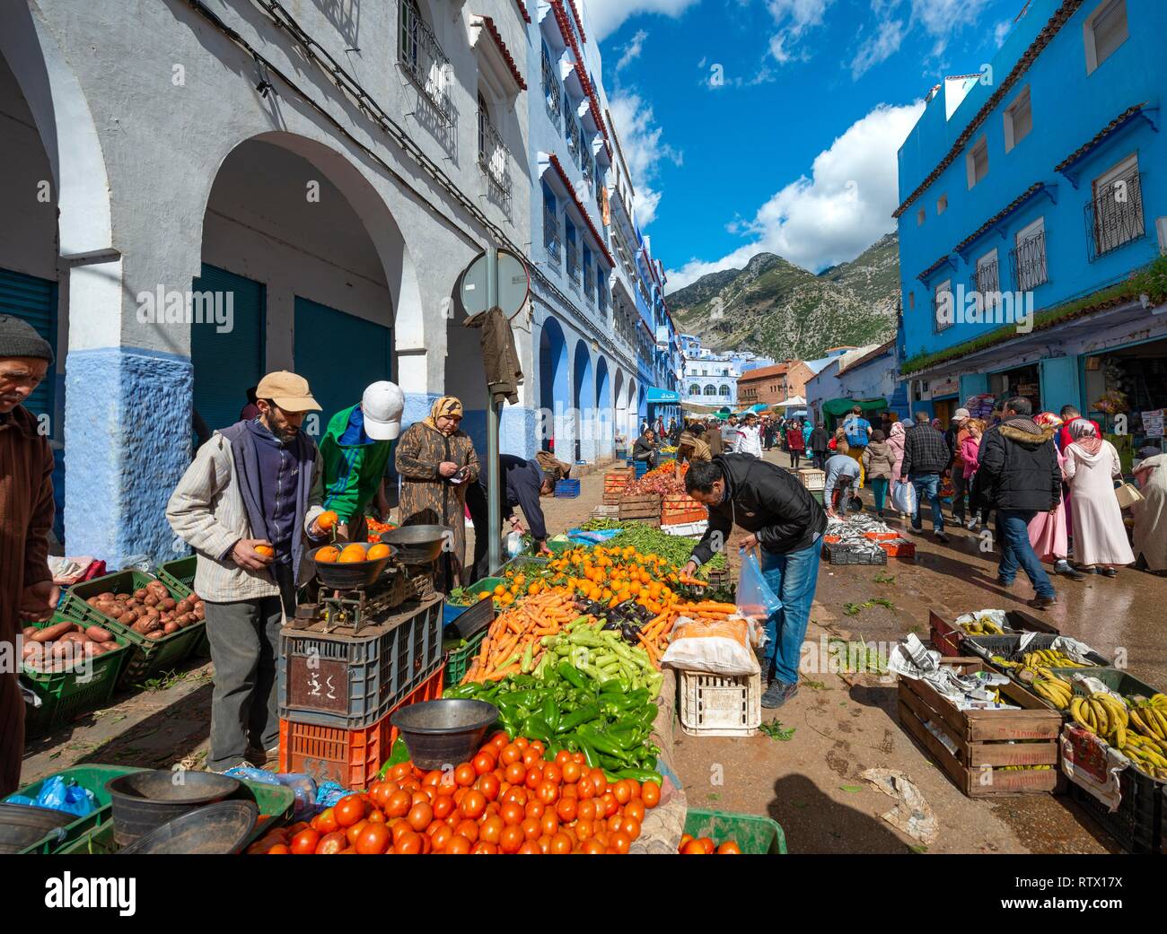 Locals shopping for vegetables and fruit, market in front of blue ...