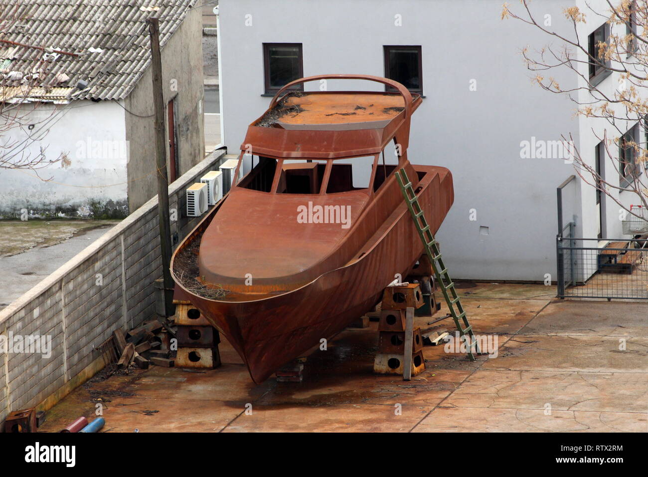 Fully rusted metal small sea boat put in backyard on strong supports to ...