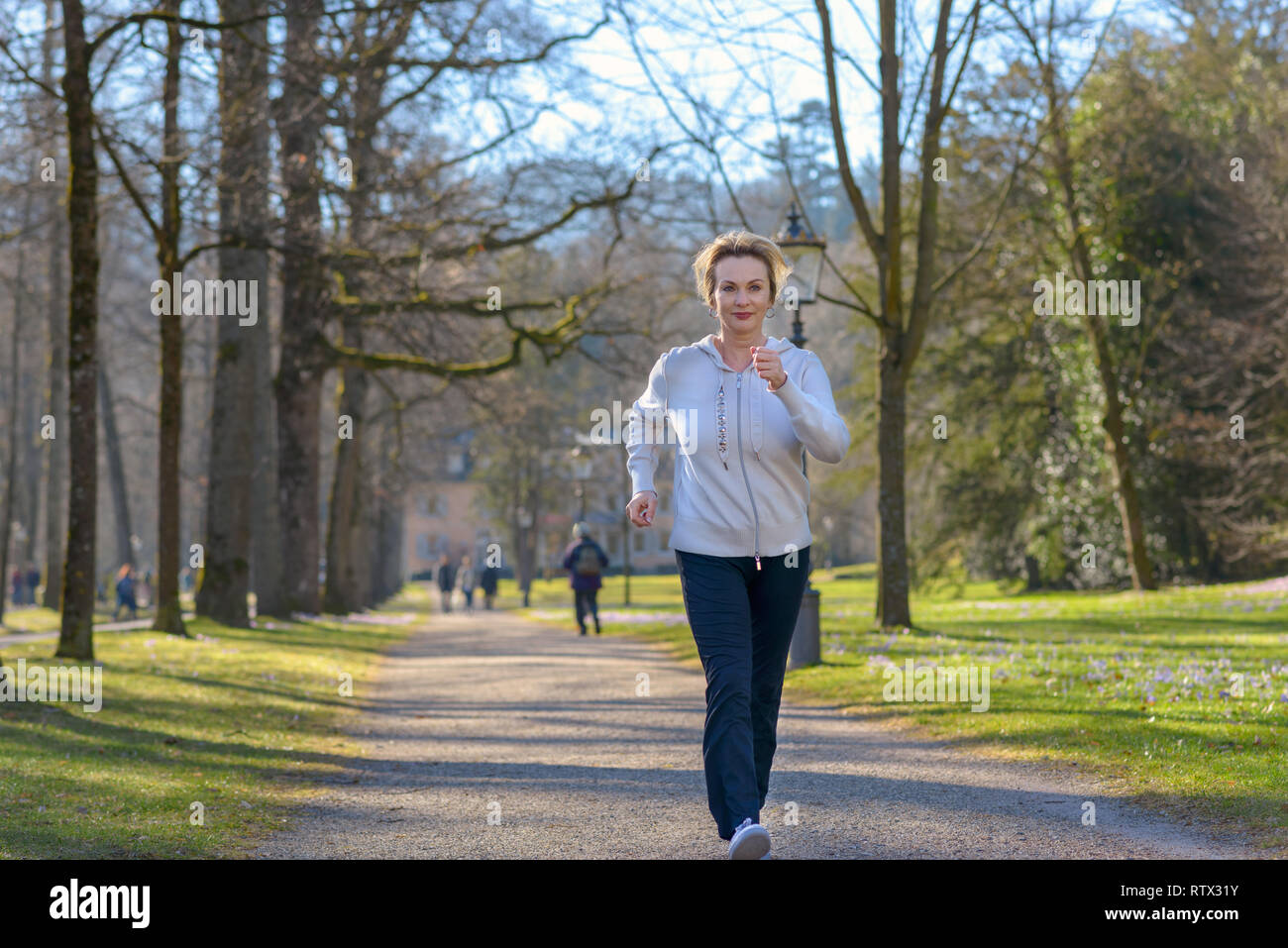 Attractive mature woman taking her daily jog through a wooded park ...