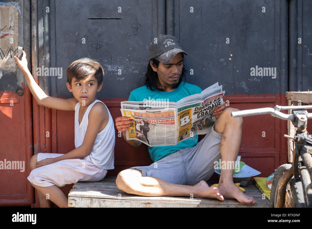 A Filipino man reads a paper whilst sitting down within a slum area ...