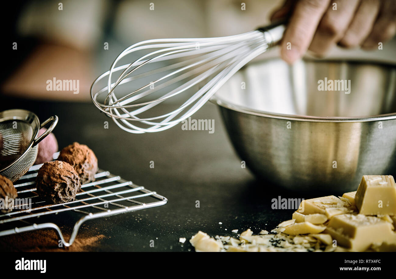 Hand of a chef holding an old metal whisk over a stainless steel mixing ...