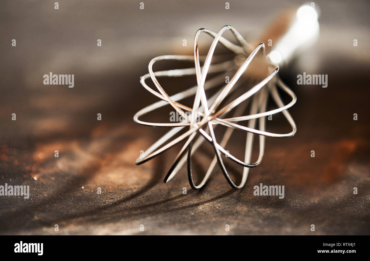 Old vintage steel wire whisk on a rustic wooden kitchen table in a ...