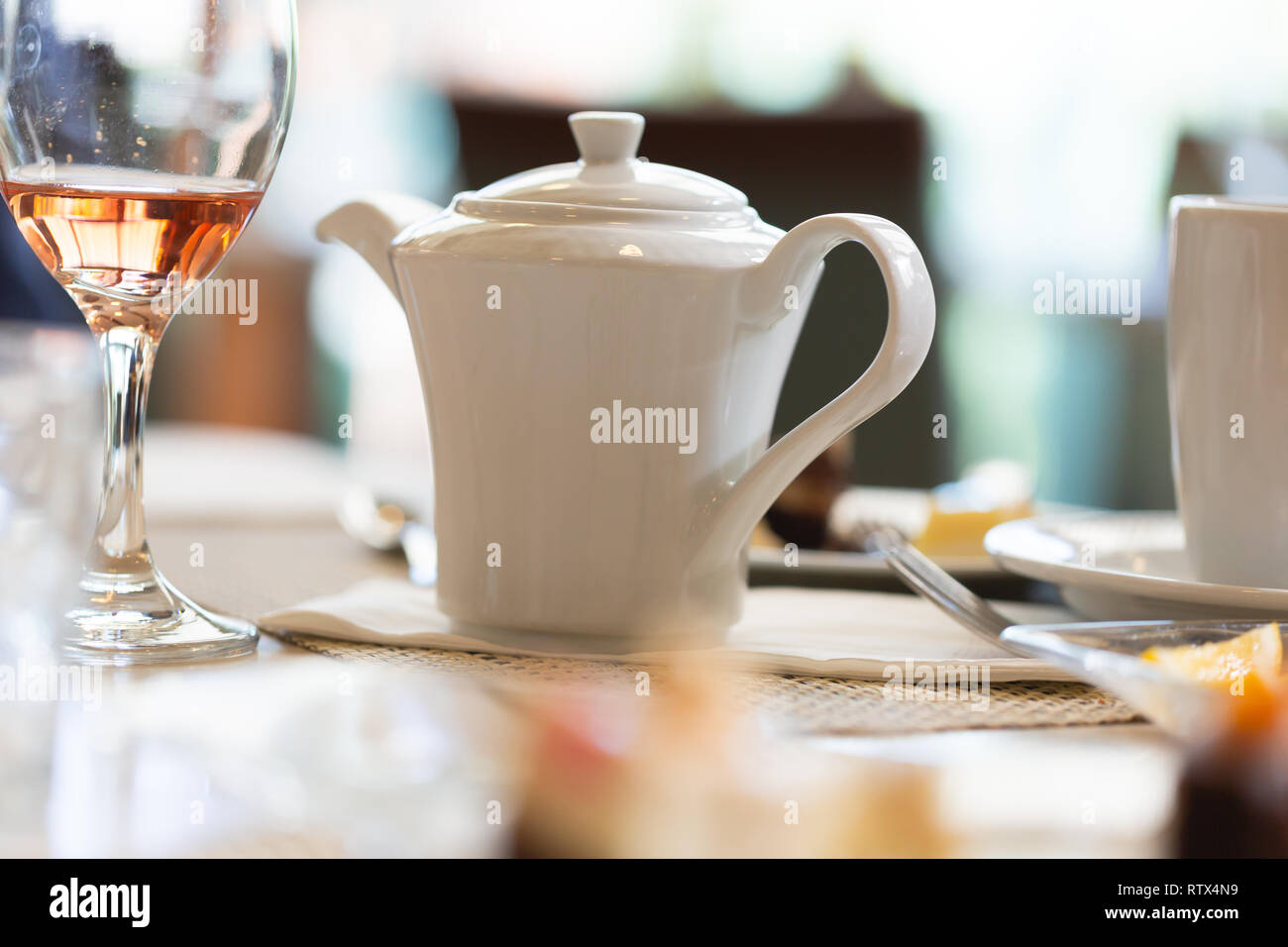Teapot on table in luxury restaurant next to glass with rose wine. Low ...
