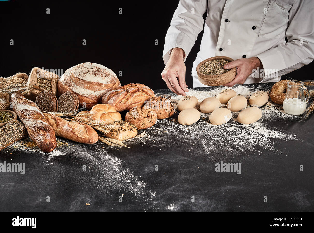 Baker sprinkling seeds or crushed wheat onto dough ready formed into ...