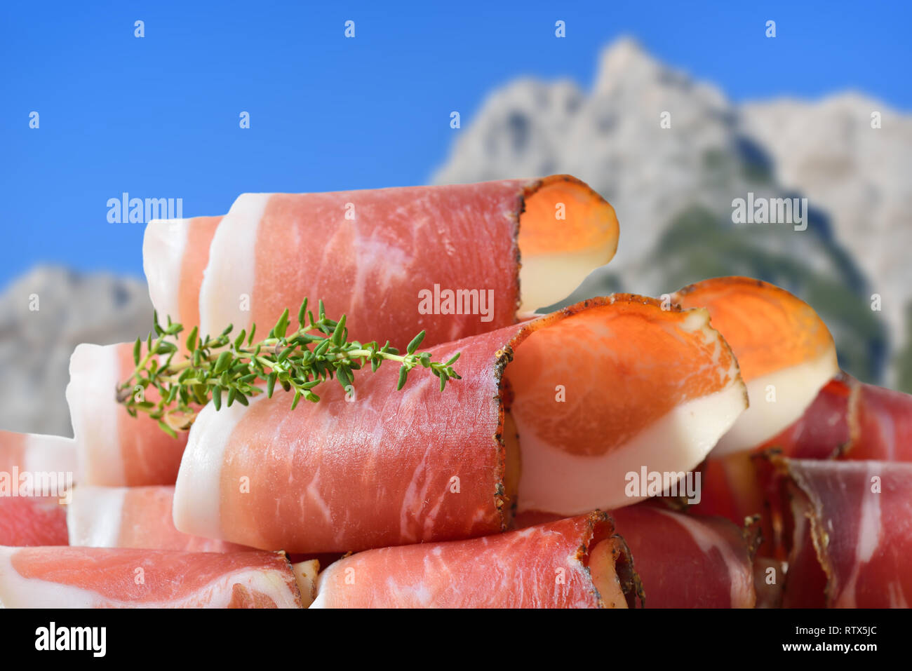 Sliced typical South Tyrolean bacon lying in front of mountains of the ...