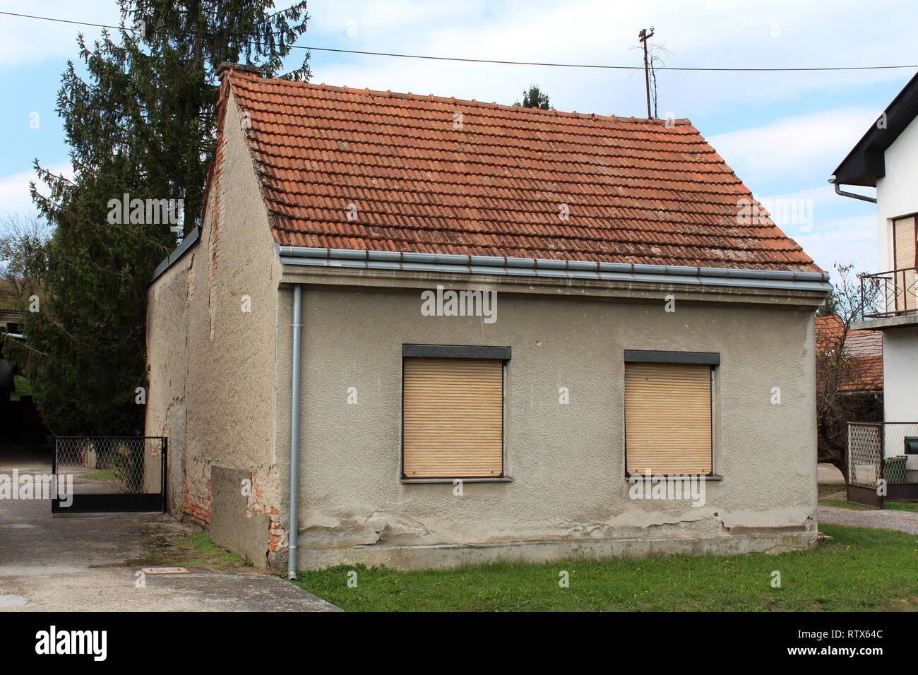 Small abandoned family house with dilapidated facade and two front windows covered with window ...